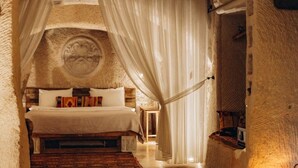 Quarto com paredes de pedra, uma cama, uma mesinha e uma banheira.