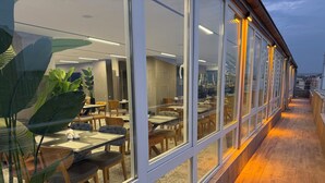 Restaurante com grandes janelas, piso de madeira e plantas em vasos.