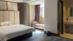 Quarto de hotel com cama, cadeira junto à janela, espelho e porta para um banheiro.
