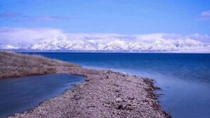 Uma costa rochosa com vista clara para montanhas nevadas ao longe.