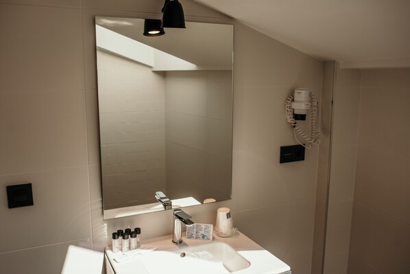 Uma casa de banho moderna com um espelho grande, uma pia, um secador de cabelo e produtos de higiene na bancada.
