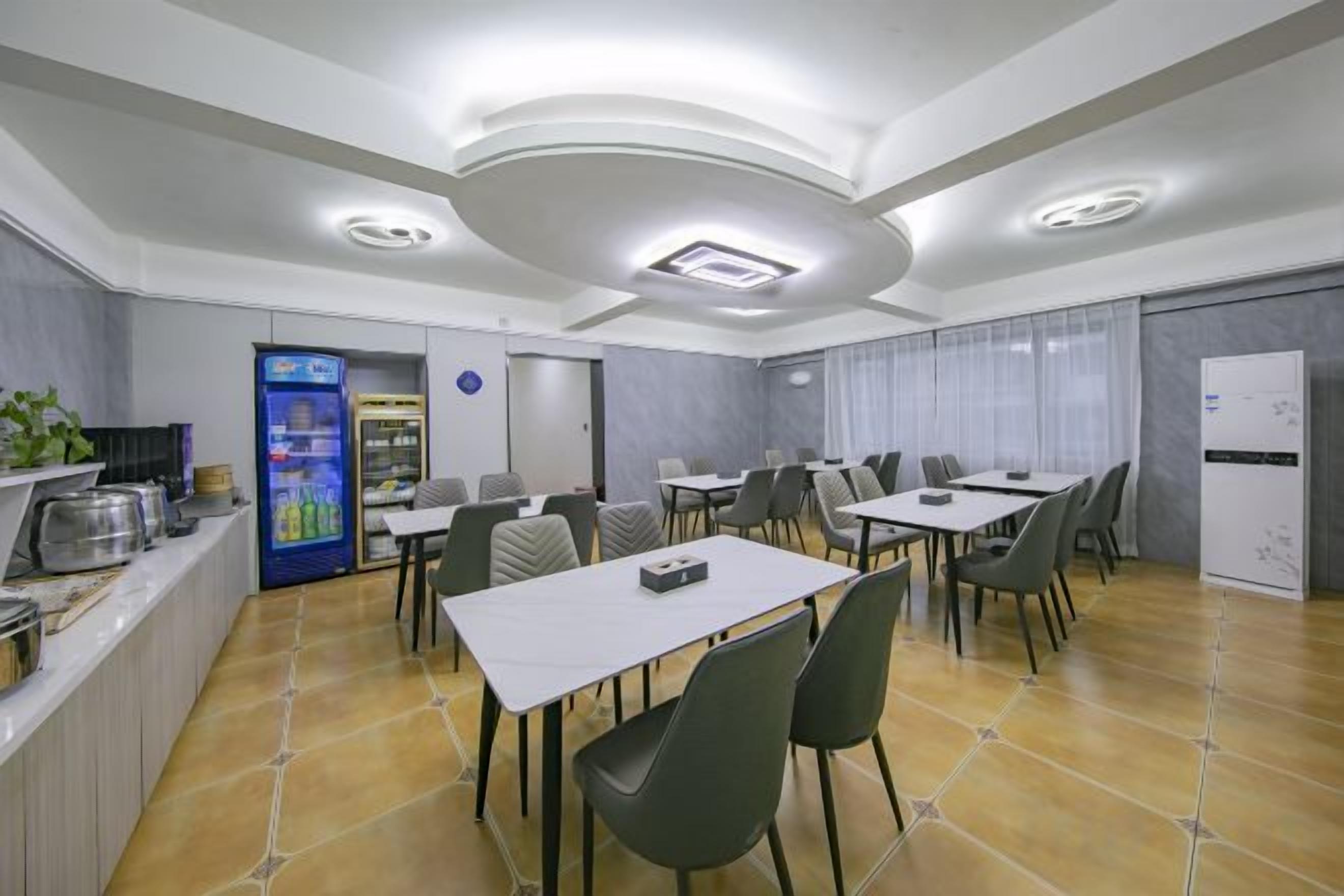Uma área de refeições moderna, com mesas, cadeiras, bancada de cozinha e geladeira.