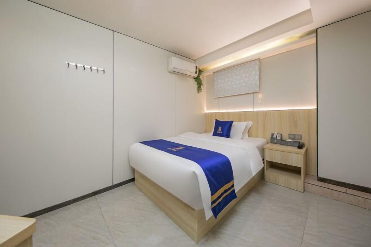 Quarto de hotel moderno com uma cama grande, uma mesa de cabeceira, um ar condicionado e um candeeiro fixado na parede.