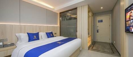 Quarto de hotel moderno com uma cama grande, uma mesa de cabeceira, uma televisão e uma porta deslizante para um banheiro.