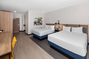 Quarto de hotel com duas camas, uma escrivaninha e uma cadeira.