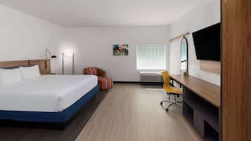 Quarto de hotel com cama, escrivaninha, cadeira, televisão, obras de arte e janela.