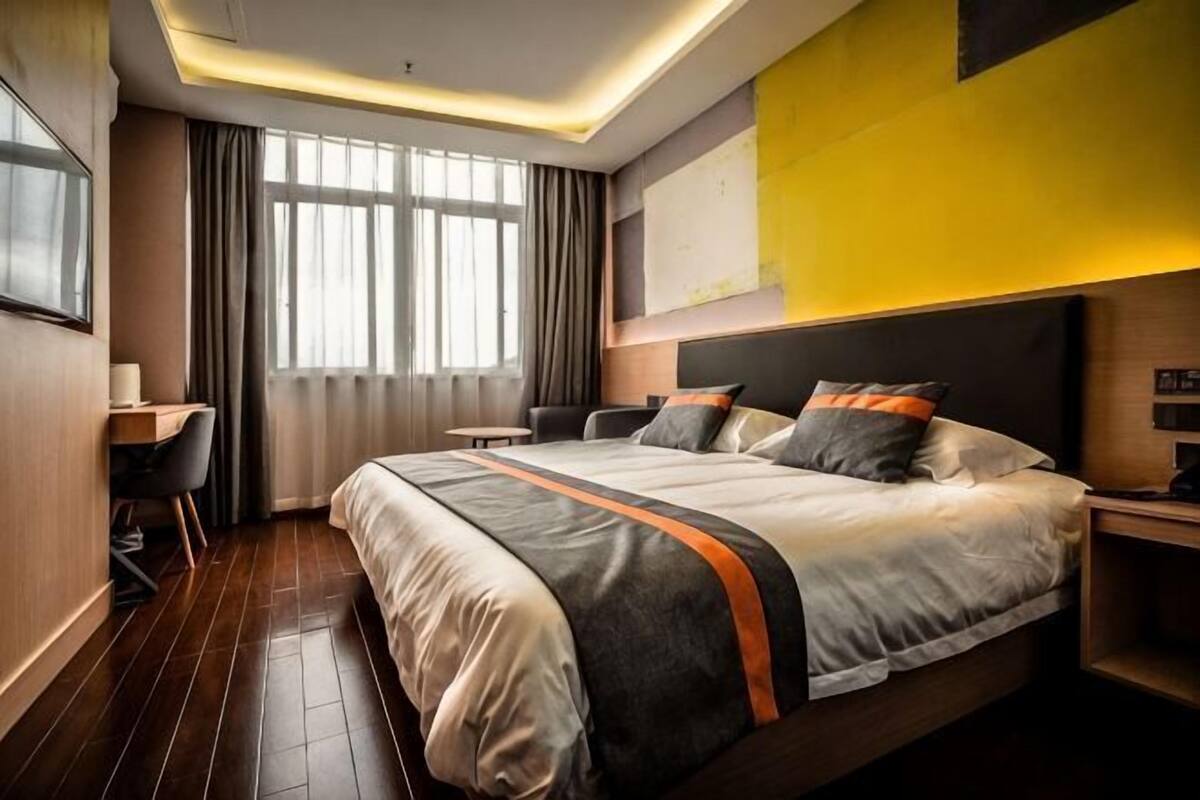 Quarto de hotel com uma cama grande, uma escrivaninha e uma janela com cortinas.