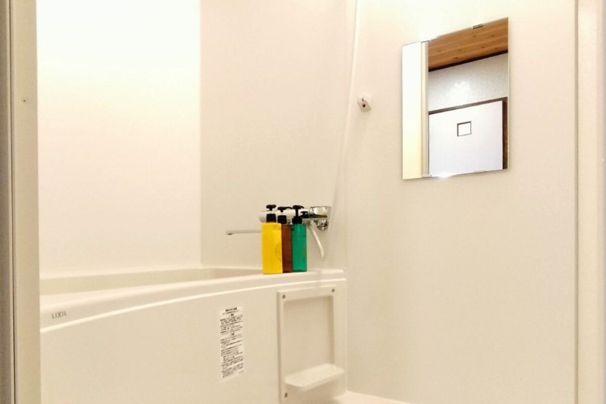 Um corredor estreito com parede branca, um pequeno armário com produtos de higiene e um espelho na parede.
