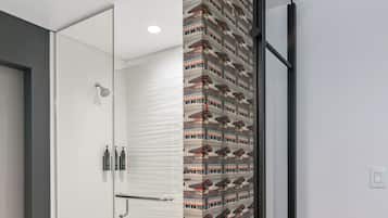 Casa de banho moderna com cabine de duche em vidro, parede revestida a azulejos brancos e design de parede estampado.