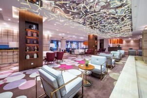 Um hall de hotel moderno com áreas de estar, balcão de recepção e bar.