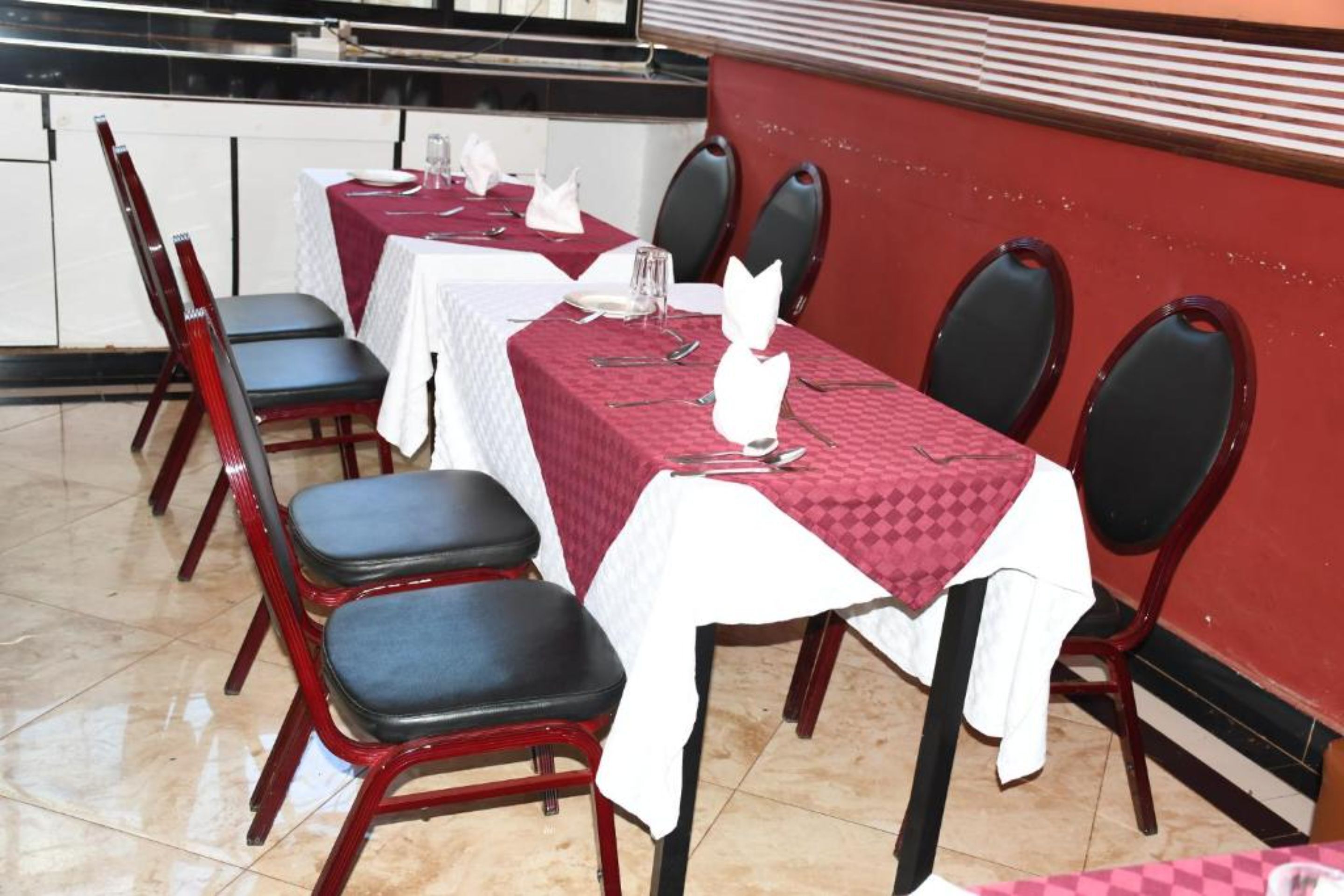 Uma área de refeições com mesas para quatro pessoas, cada uma com toalha de mesa vermelha e guardanapos brancos.