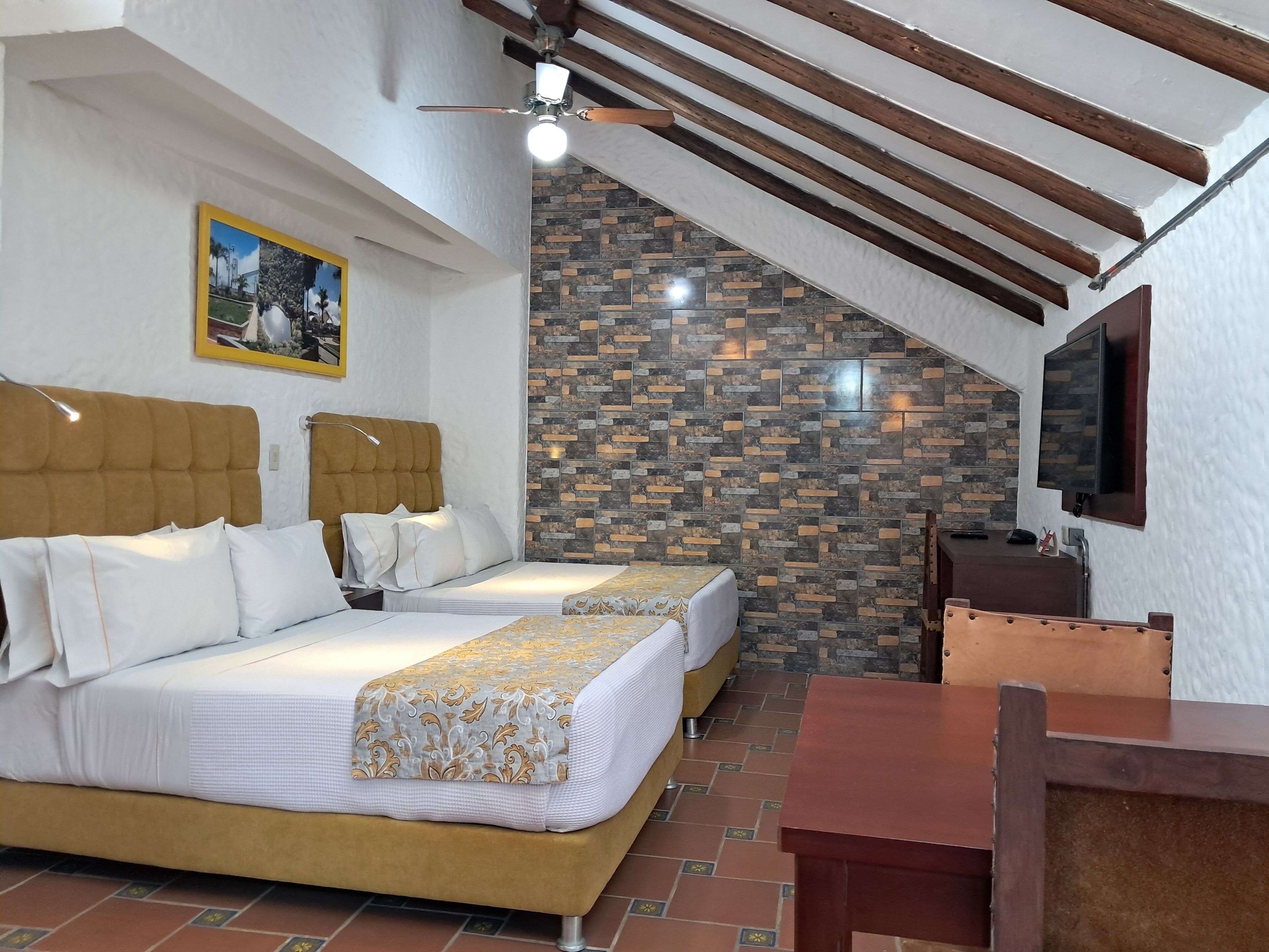 Quarto com duas camas, teto de madeira, parede de pedra e televisão fixada na parede.