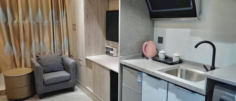 Uma cozinha moderna com micro-ondas embutido, pia e um pequeno espaço de estar com uma cadeira e mesa lateral.
