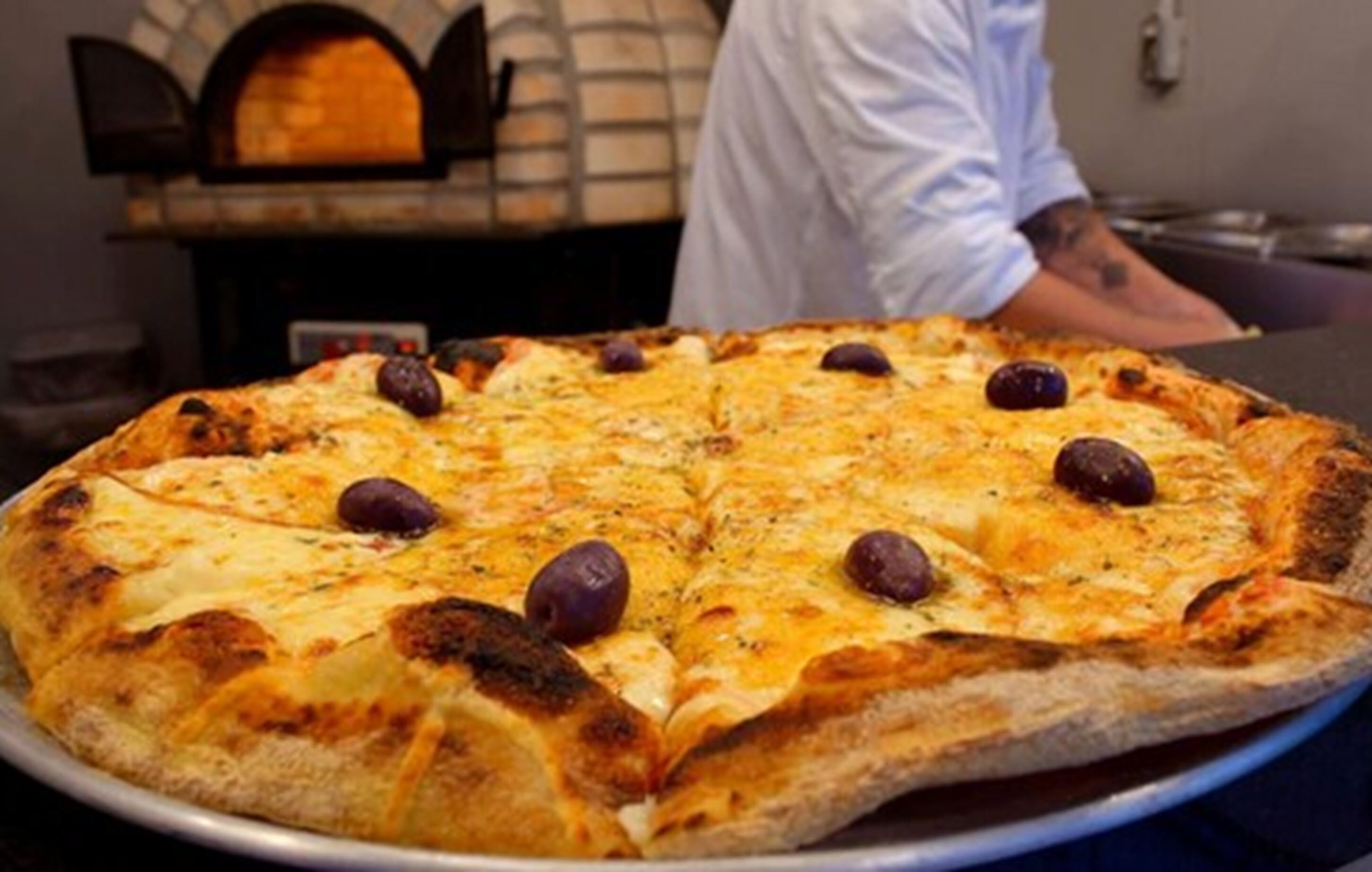 Uma pizza grande com azeitonas em uma bandeja de metal.