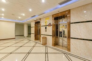 Um hall de hotel com piso de mármore, balcão de recepção e elevador de vidro.
