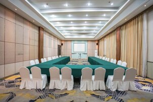 Uma sala de conferências com uma longa mesa, cadeiras brancas e uma tela de projetor.