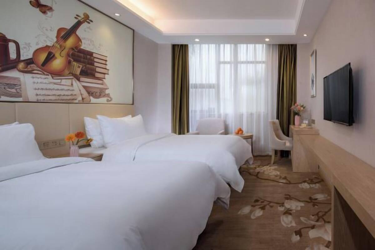 Quarto de hotel com duas camas, uma escrivaninha, uma cadeira, uma televisão e um mural na parede.