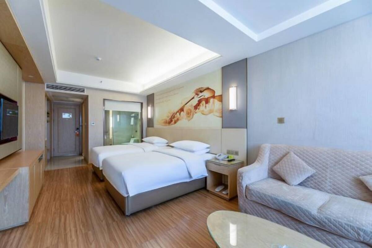 Quarto de hotel com cama, sofá, televisão e um quadro na parede.