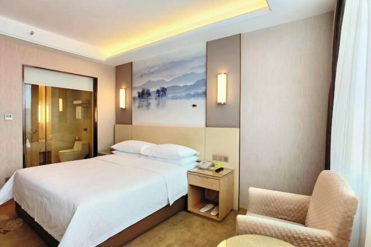 Quarto de hotel com cama, mesa de cabeceira, luminária, cadeira e um quadro na parede.