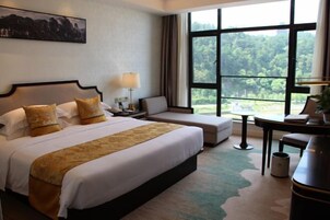 Quarto de hotel com uma cama grande, um sofá, uma escrivaninha e vista para o exterior.