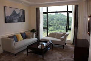 Uma sala de estar com sofá, poltrona, mesa de centro e uma janela grande com vista para o verde.