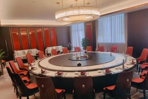 Sala de conferências com mesa redonda, cadeiras vermelhas e um lustre moderno.