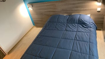 Cama com colcha azul em quarto com paredes verde-água e piso de madeira.