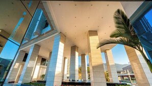 Um edifício moderno com grandes colunas, uma fonte central e uma palmeira.
