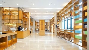 Interior moderno de biblioteca com estantes de madeira, balcão de atendimento e área de estar central.