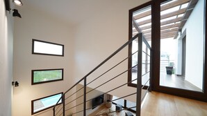 Uma escadaria moderna com degraus de madeira e guarda-corpos de metal, que dá acesso a uma varanda com vista para o exterior.