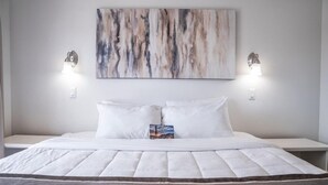 Cama bem arrumada com cobertura acolchoada, duas luminárias de cabeceira e um quadro abstrato grande acima.