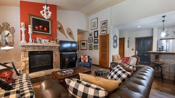Uma sala de estar com lareira, televisão, sofá com almofadas xadrez e área de jantar com balcão.