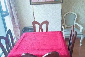 Quarto com colcha vermelha, duas cadeiras de madeira, uma cadeira branca e uma pequena mesa com abajur.