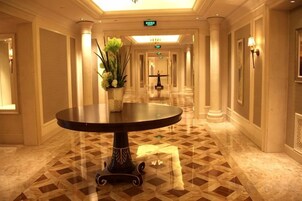 Corredor de hotel com uma mesa redonda, colunas e piso estampado.