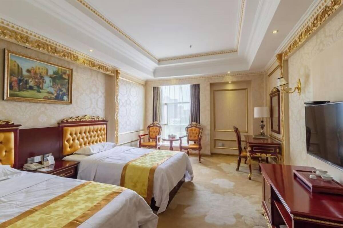 Quarto de hotel com duas camas, televisão, um quadro e vista da cidade pela janela.