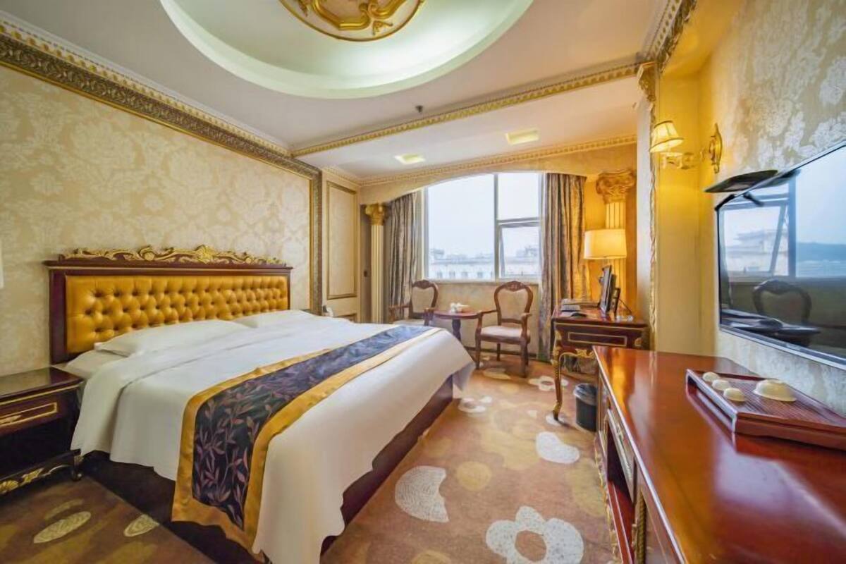 Quarto de hotel com uma cama grande, uma escrivaninha com cadeira, televisão e janela com vista.
