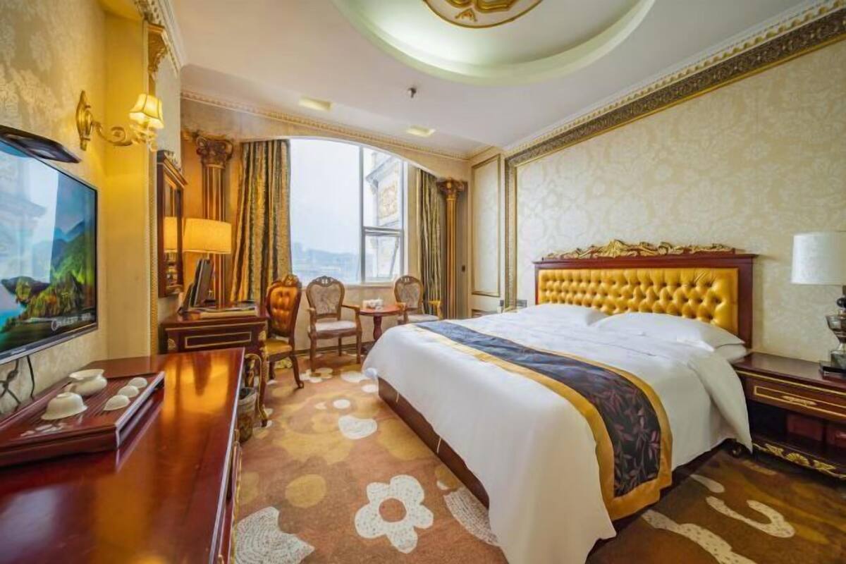 Um quarto de hotel luxuoso com uma cama grande, uma mesa de escritório com um computador, uma TV e vista para a cidade.