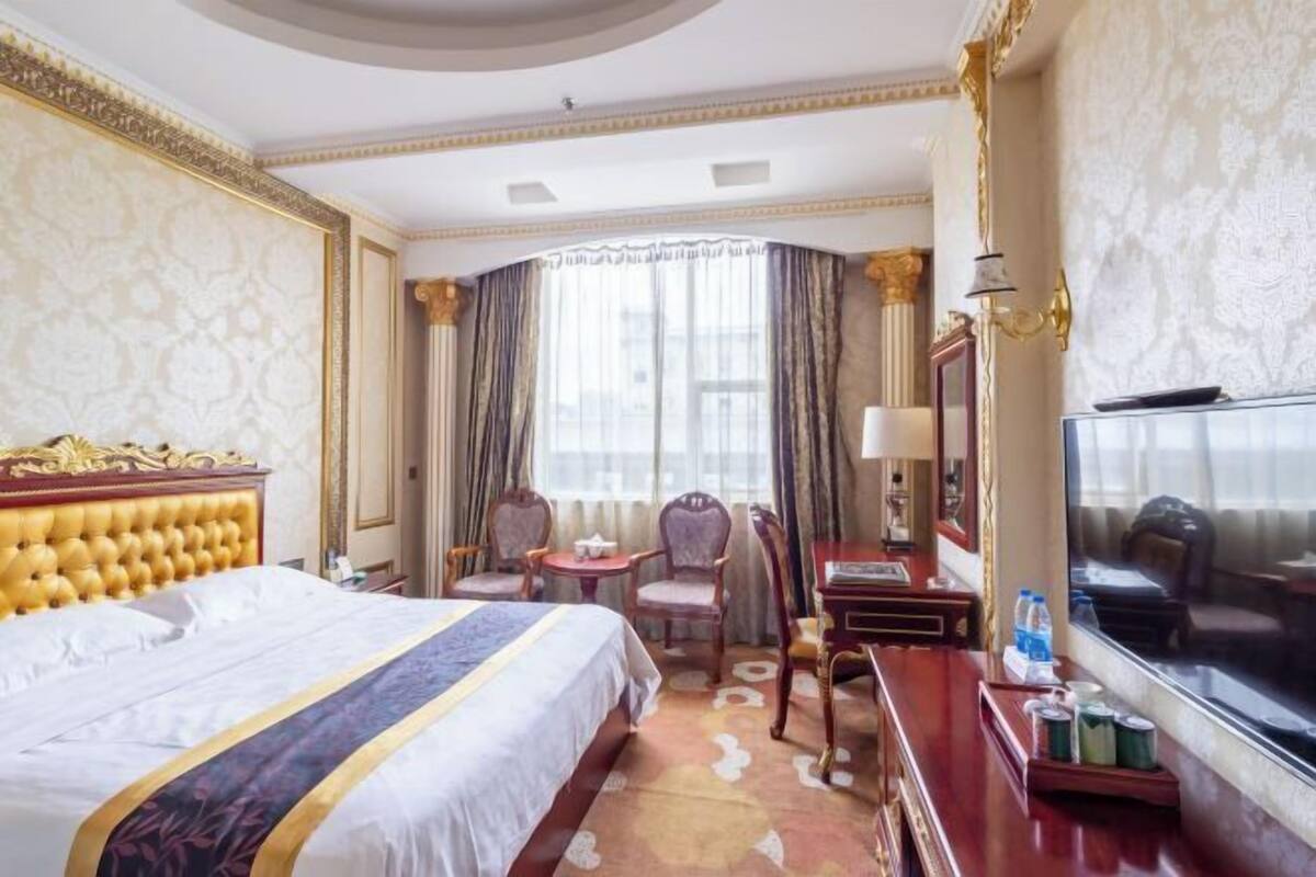 Quarto de hotel com uma cama grande, uma escrivaninha com cadeira, televisão e janela com cortinas.