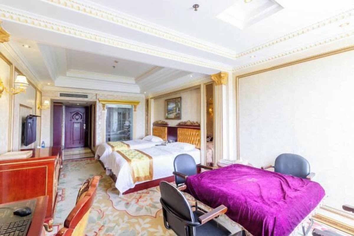 Quarto de hotel com duas camas, uma escrivaninha, uma cadeira e uma televisão.