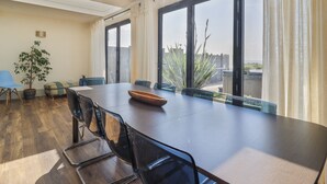 Quarto espaçoso com uma grande mesa, cadeiras, um vaso de planta e vista através de amplas janelas.