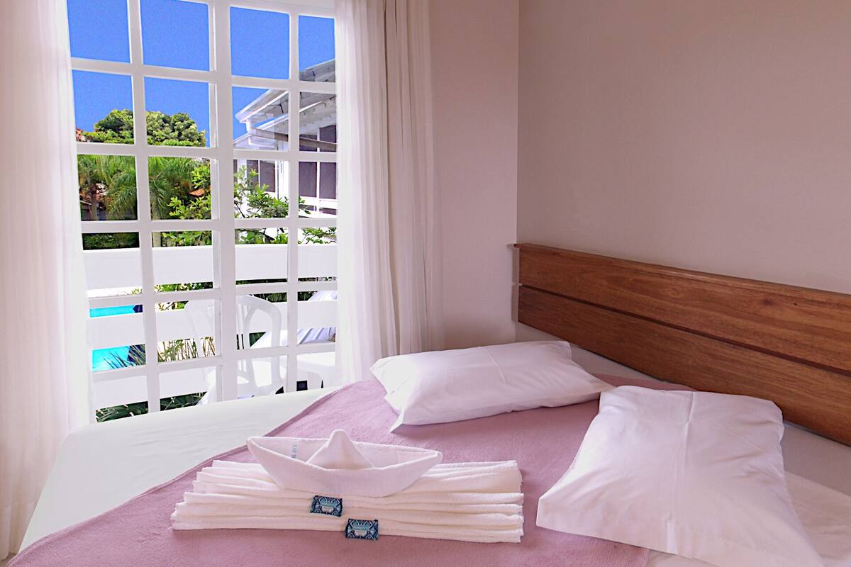 Quarto de hotel com cama, janela com cortinas e vista para o exterior.