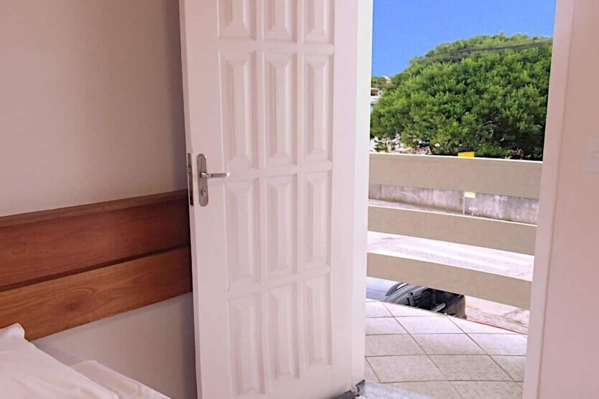 Quarto de hotel com cama, porta para uma varanda e vista para uma colina verde.