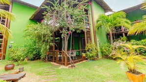 Um edifício verde com um pátio coberto, rodeado por vegetação exuberante e plantas em vasos.