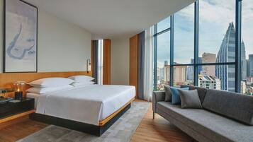 Quarto de hotel moderno com uma cama grande, um sofá e vista para a cidade.