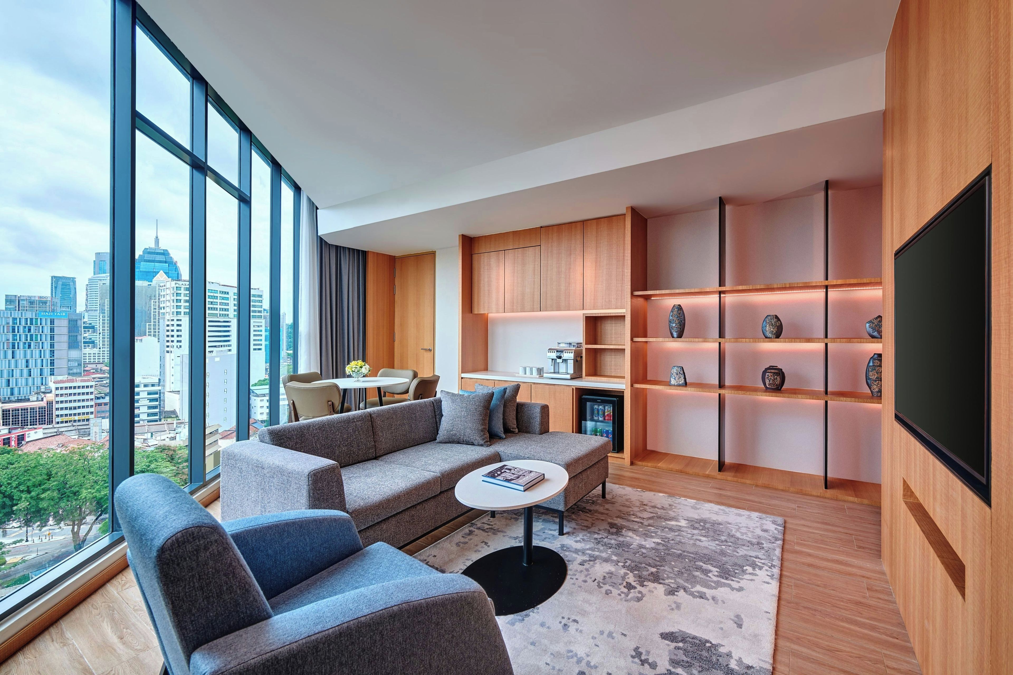 Sala de estar moderna com sofá, mesa de centro e vista para a cidade através de grandes janelas.