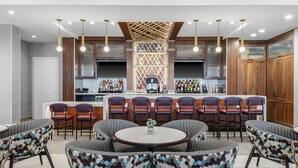 Uma área de bar moderna com balcão central, diversas opções de assento incluindo banquetas e mesas redondas, e um teto decorativo.
