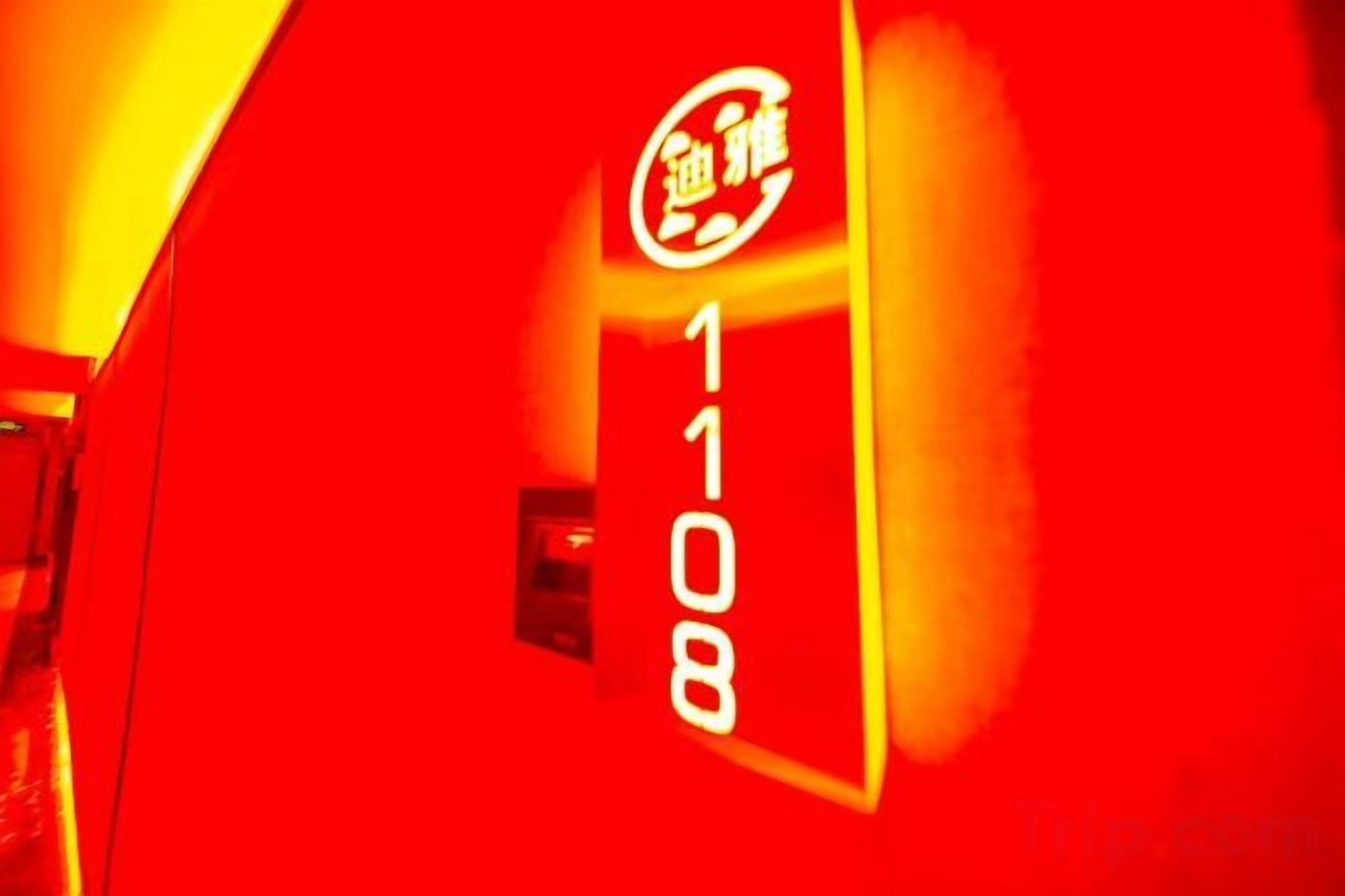 Pared vermelha com um número de porta 1108 e um logotipo circular acima.