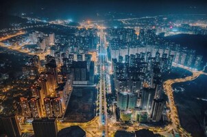 Vista aérea noturna de uma área urbana densamente povoada, com edifícios altos e ruas iluminadas.