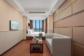Quarto de hotel com cama, sofá, mesa de centro e televisão na parede.