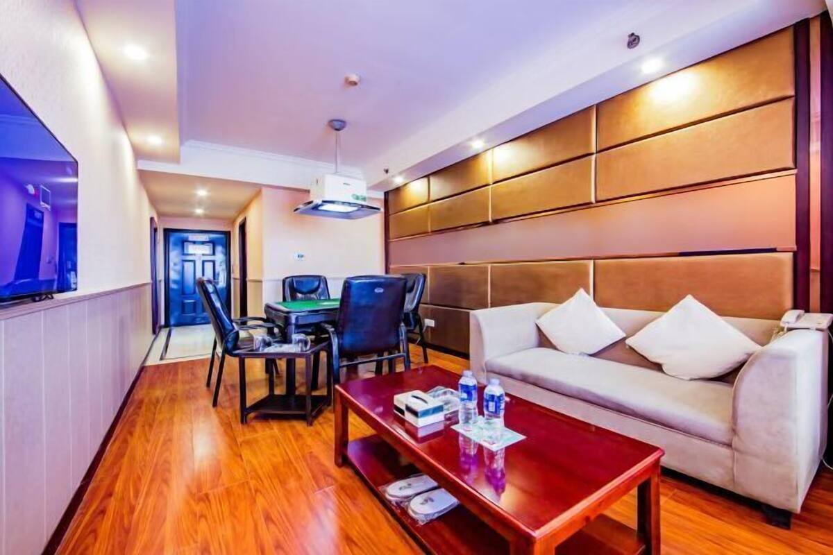 Quarto de hotel moderno com piso de madeira, sofá, mesa de centro e escrivaninha com cadeiras.